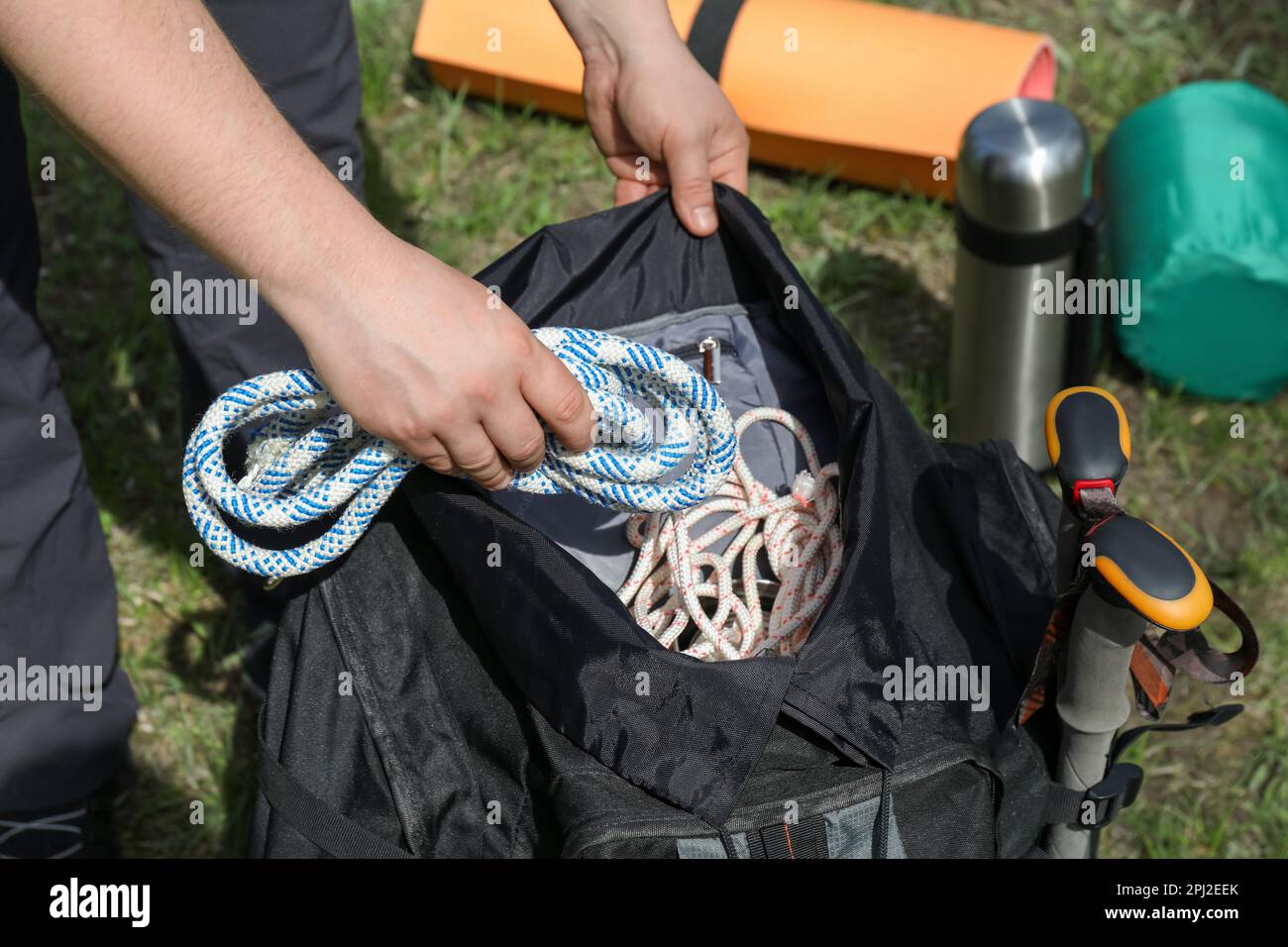 Hiker putting climbing rope into backpack outdoors, closeup. Mountain ...