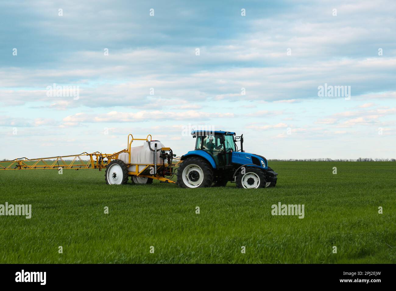 Tractor spraying pesticide in field on spring day. Agricultural ...