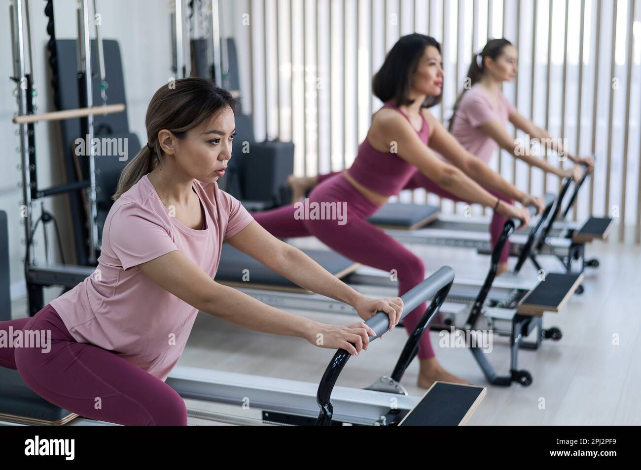 Three Asian women doing lunges on a reformer machine Stock Photo - Alamy