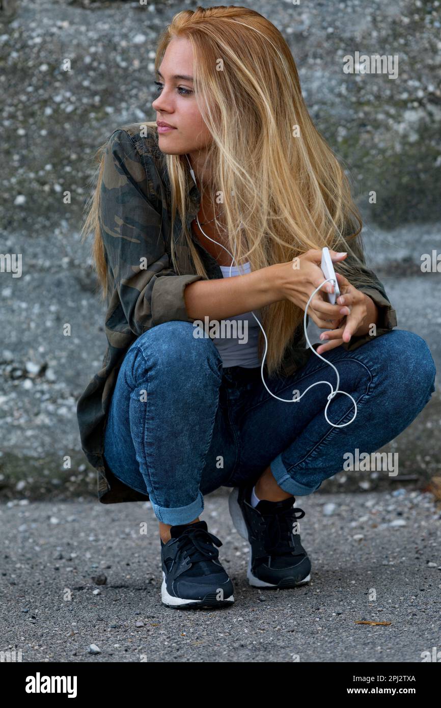 Stunning blonde girl crouching at the base of a concrete wall on the ...