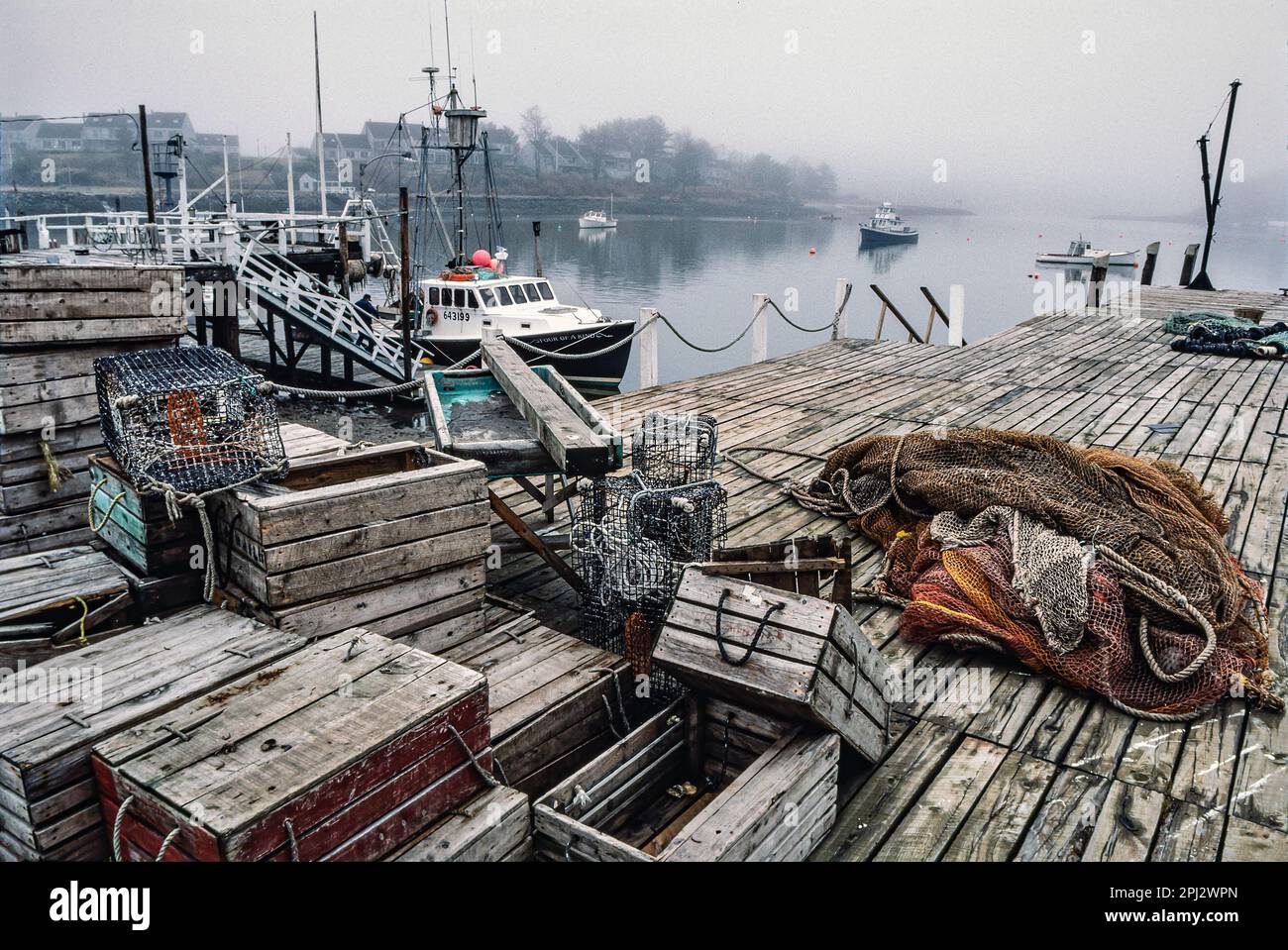 Lobster pots and netting are piled on working dock with fishing boats ...
