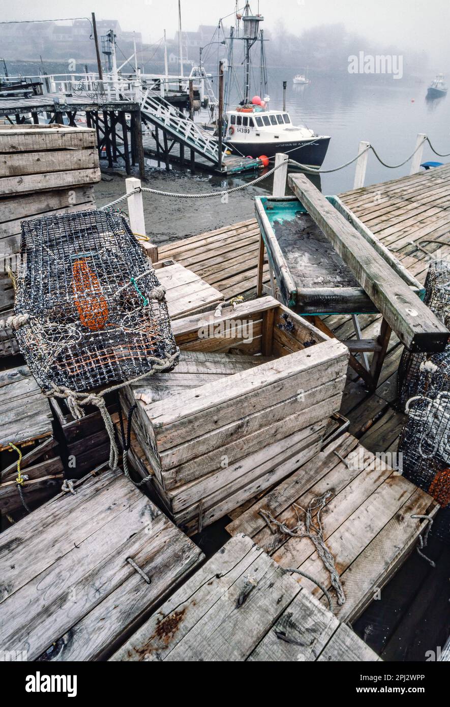 Lobster pots and netting are piled on working dock with fishing boats ...