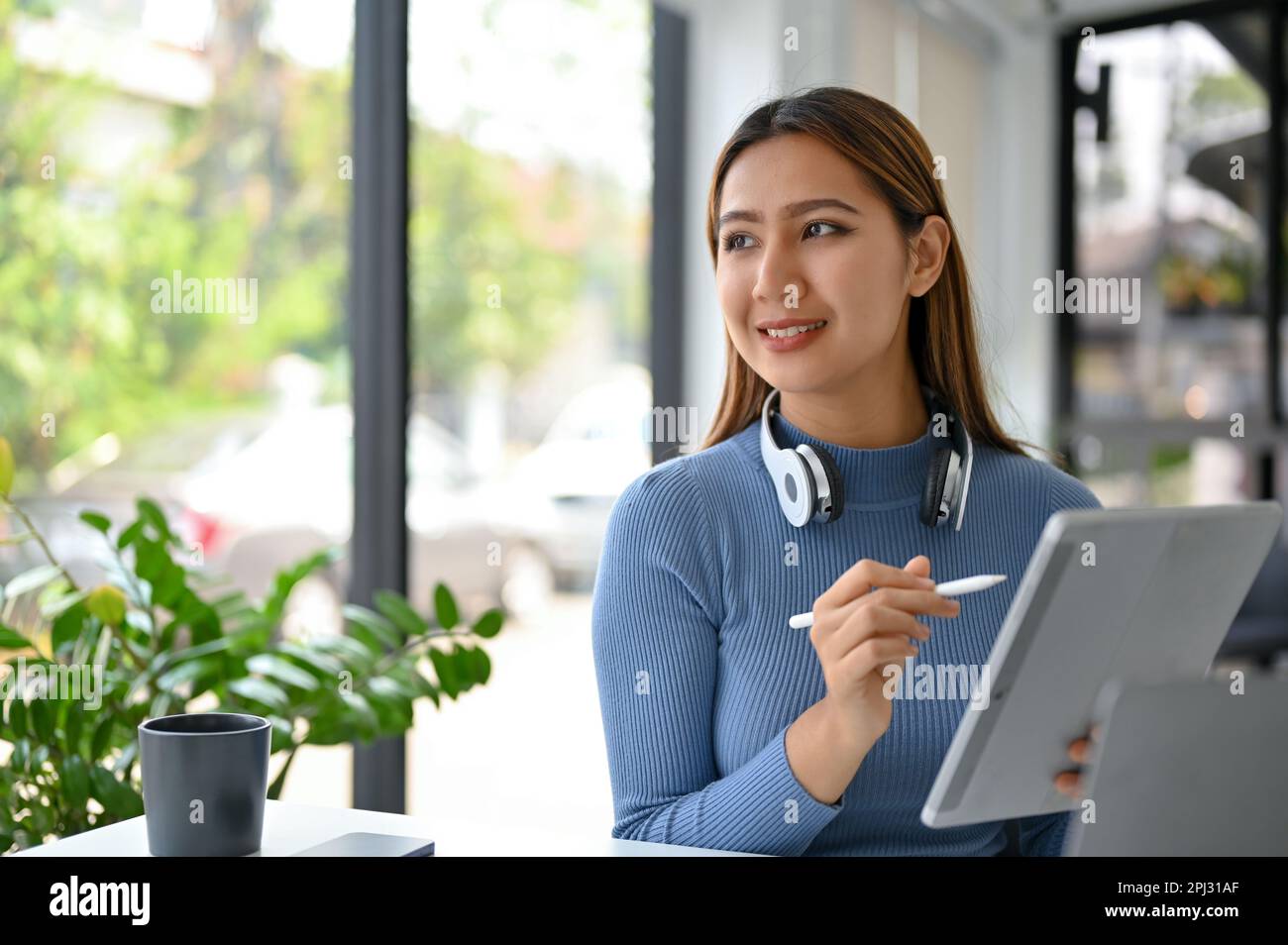 Happy millennial Asian woman sits in the cafe with her portable tablet ...