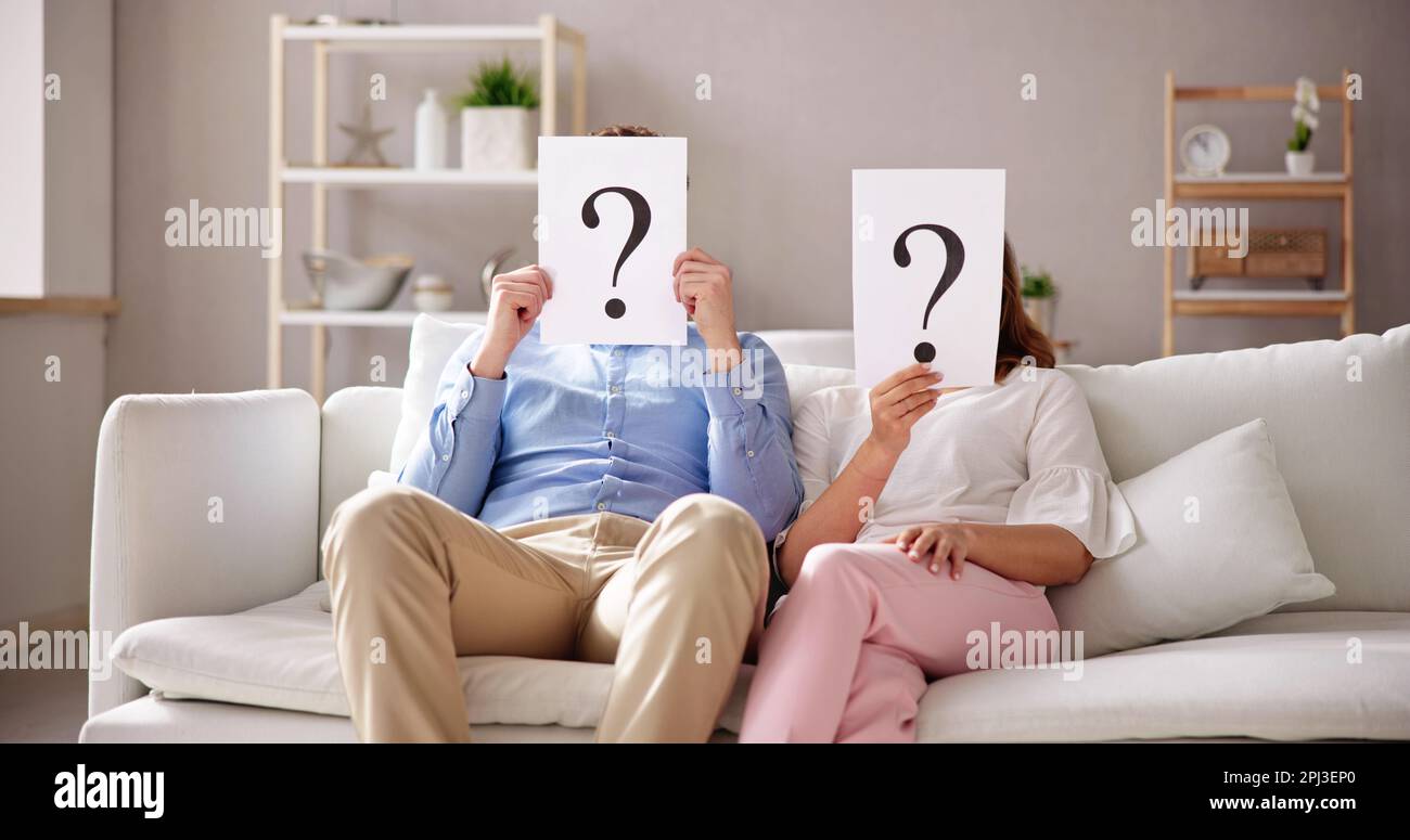 Couple Sitting On Sofa Holding Question Mark Sign In Front Of Face ...