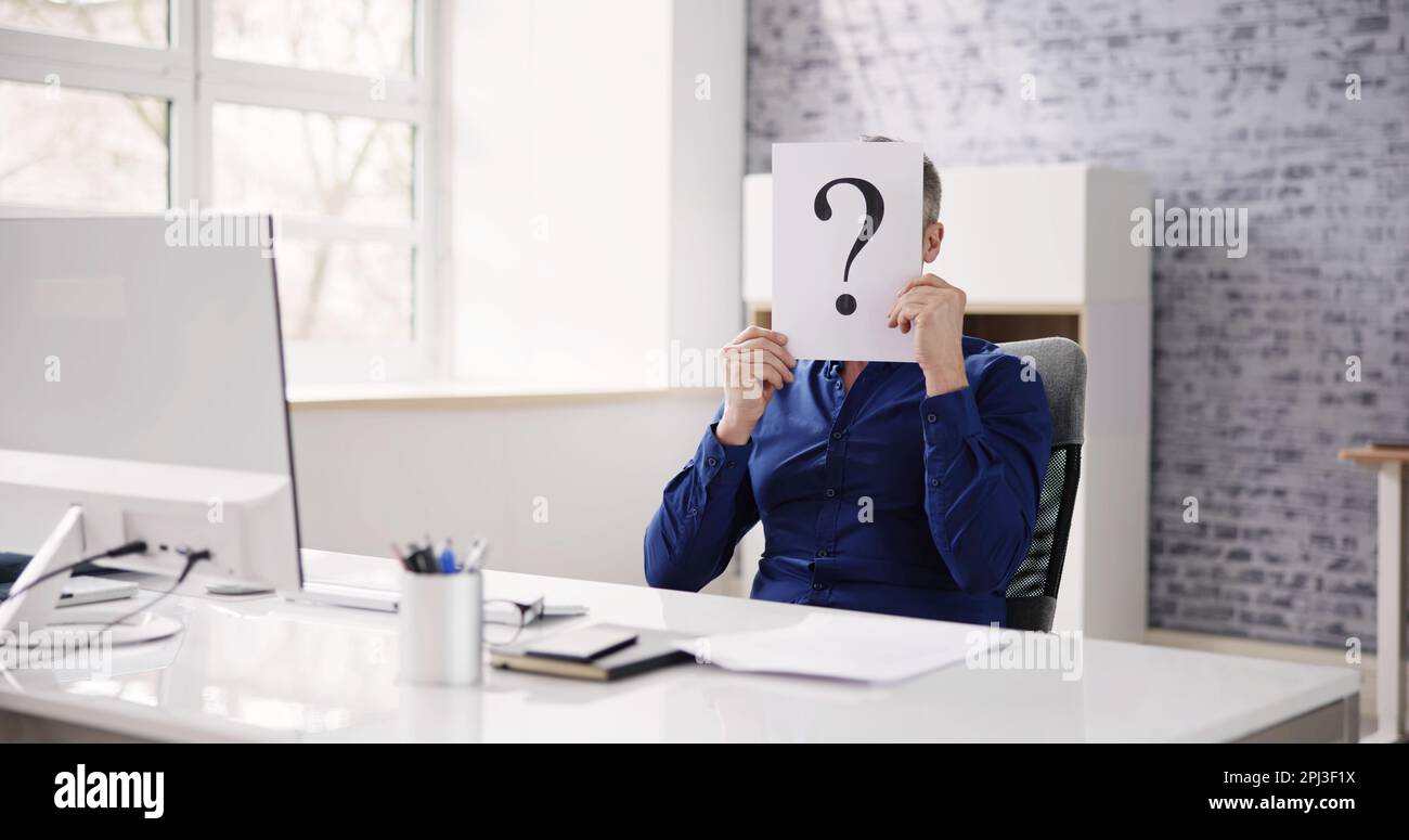 Businessman Holding Paper With Question Mark In Front Of Face At Desk ...