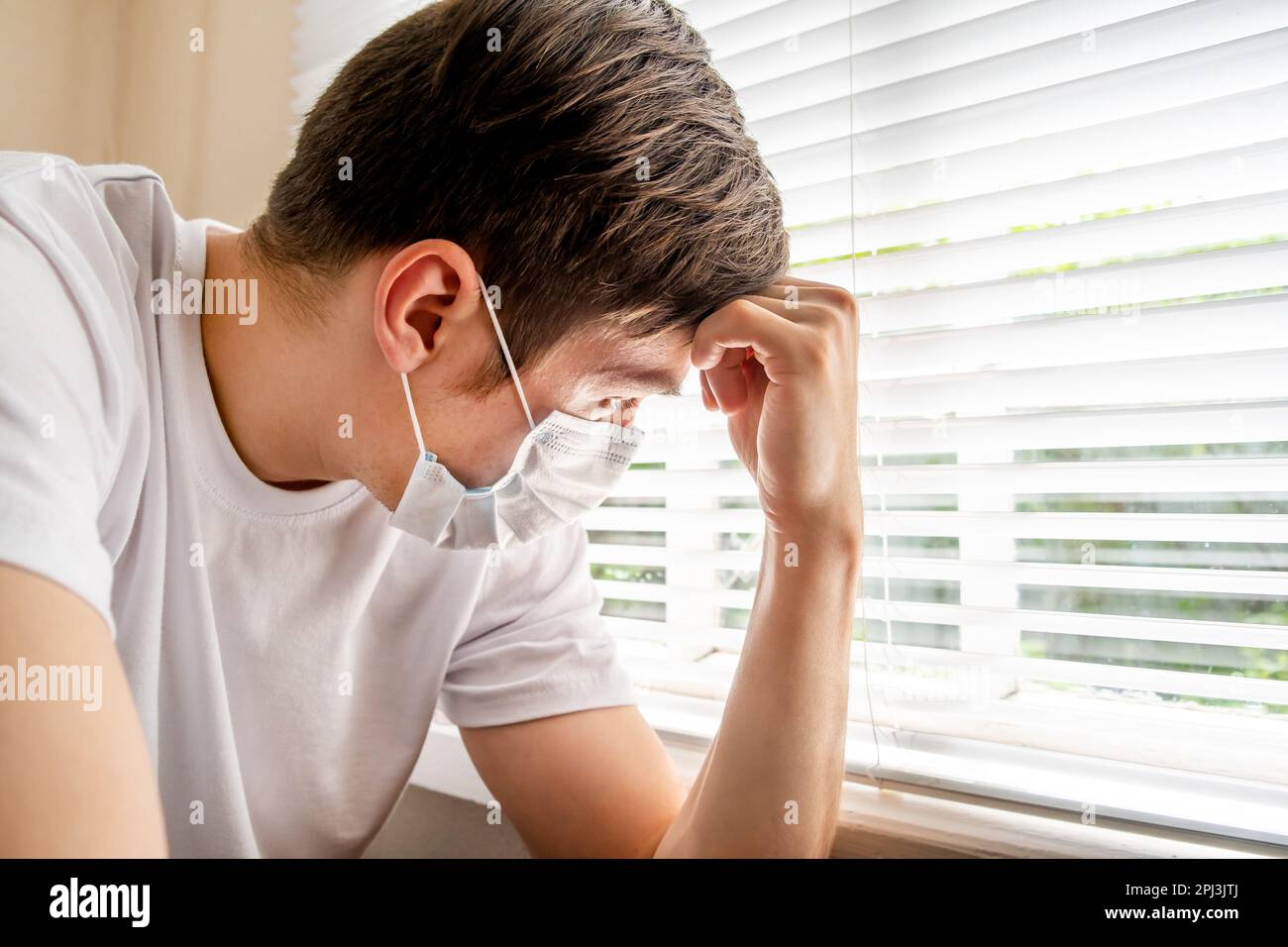 Sad Young Man in a Surgical Mask by the Window in the Room Stock Photo ...