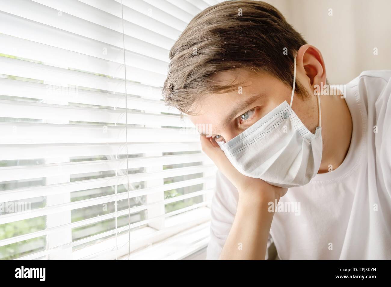 Sad Young Man in a Surgical Mask by the Window in the Room Stock Photo ...