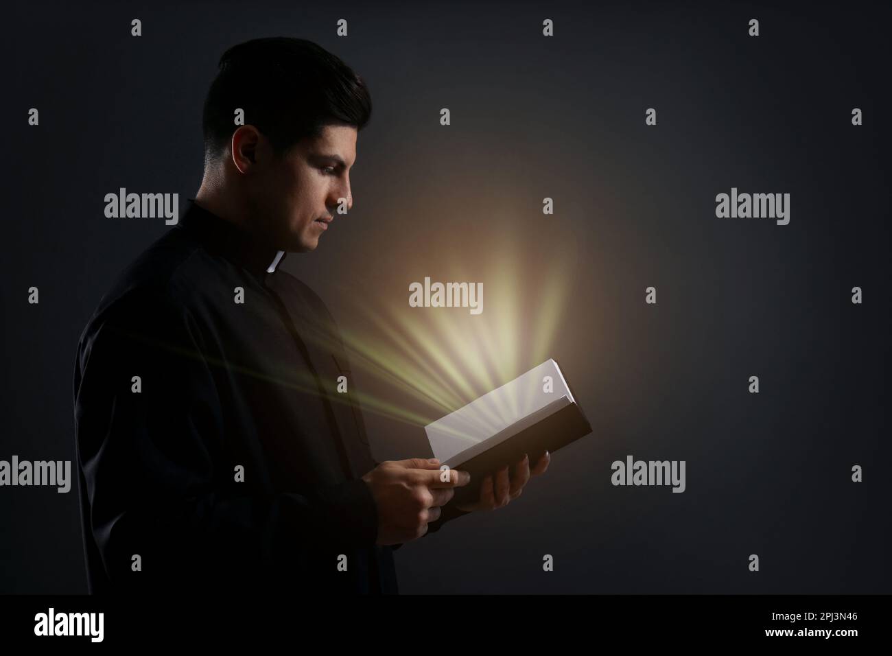 Priest holding Bible with holy light on black background Stock Photo ...