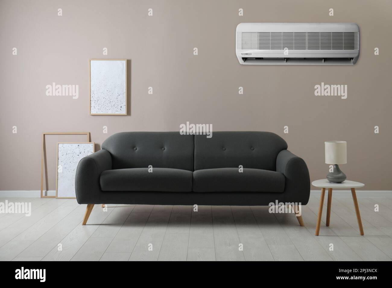 Modern air conditioner on beige wall in living room with stylish sofa ...