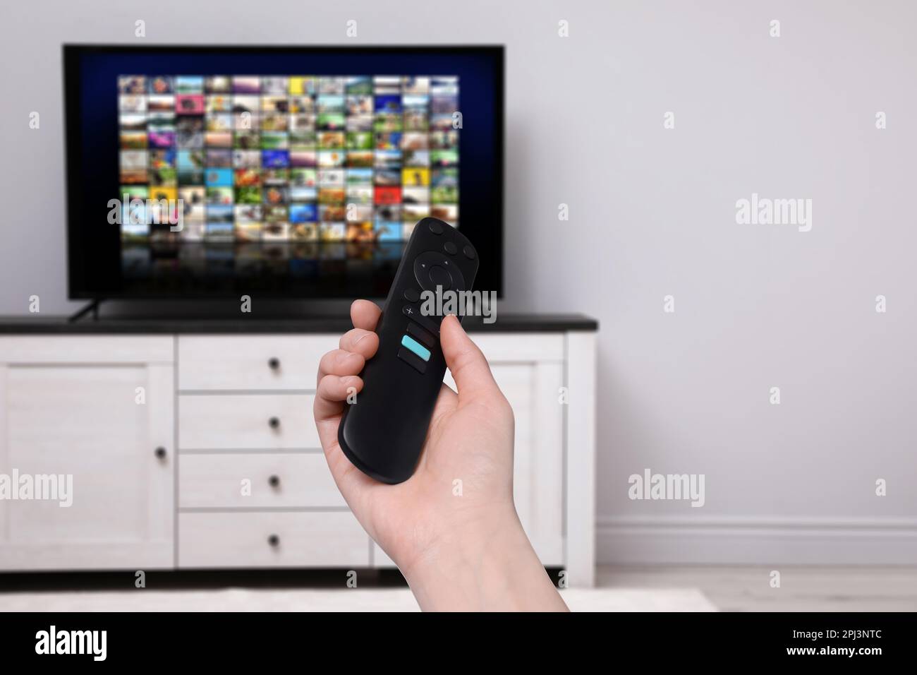 Woman with remote control changing channels while watching TV at home ...
