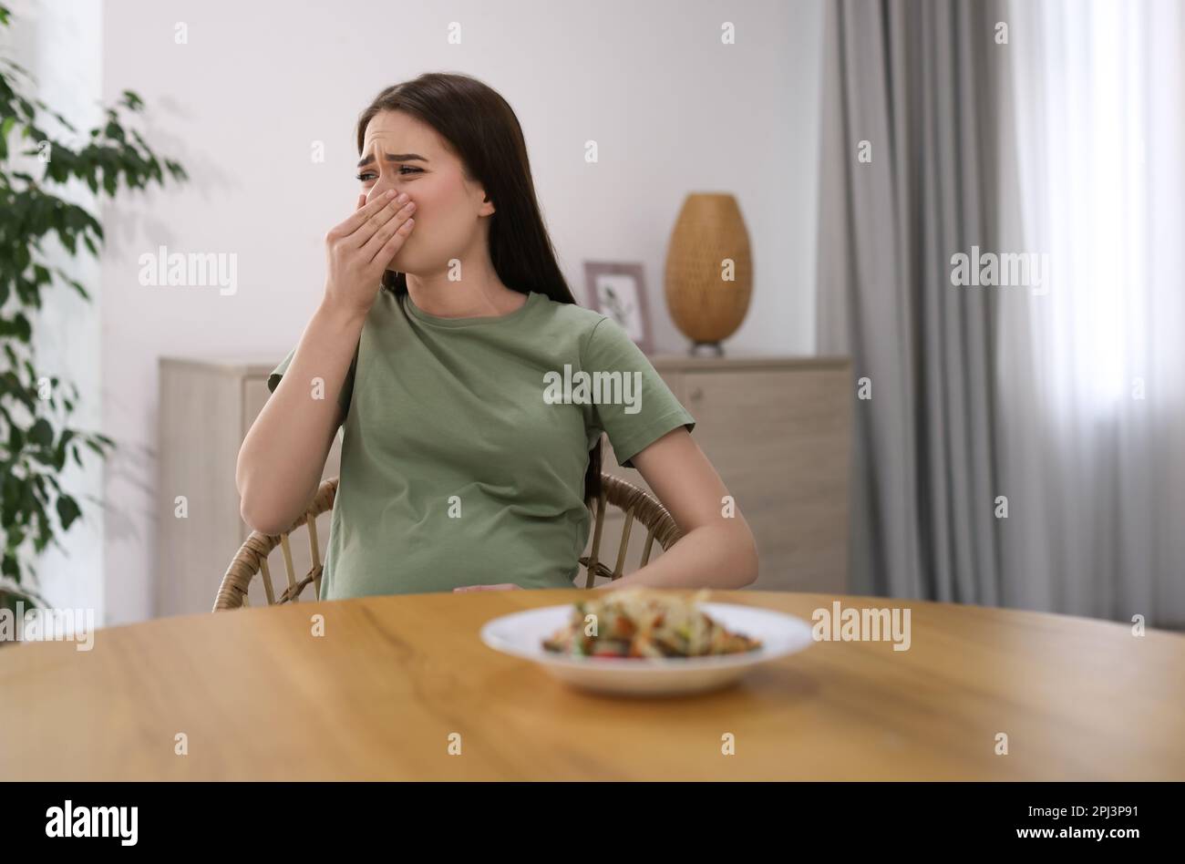 Young woman feeling nausea while seeing food at wooden table indoors ...