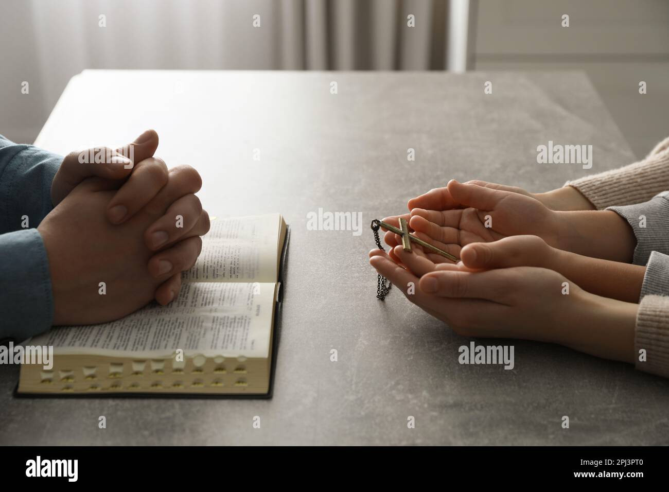 Boy praying and reading Bible with his godparents at grey table indoors ...