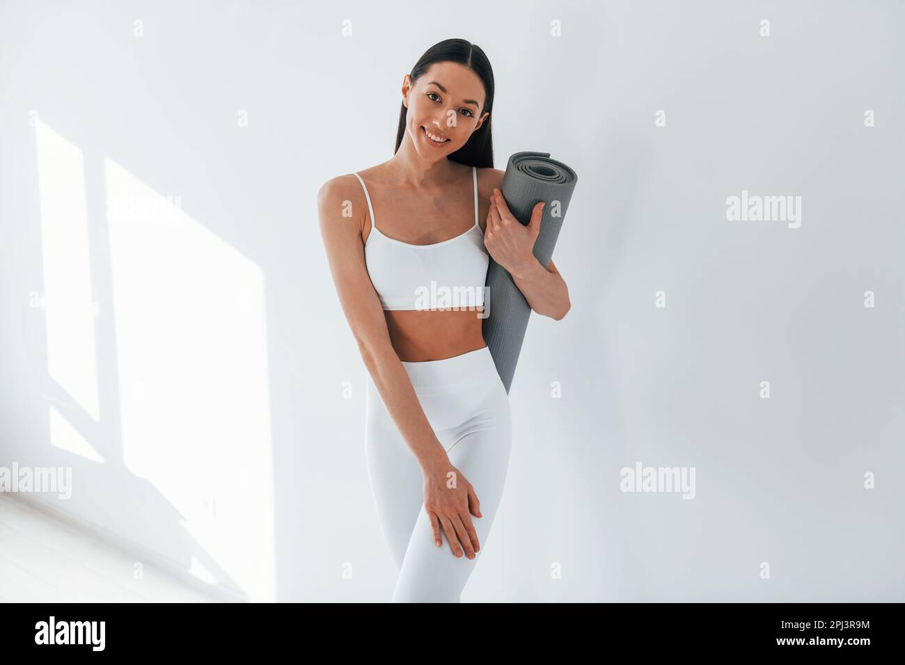 With mat in hands. Young caucasian woman with slim body shape is ...