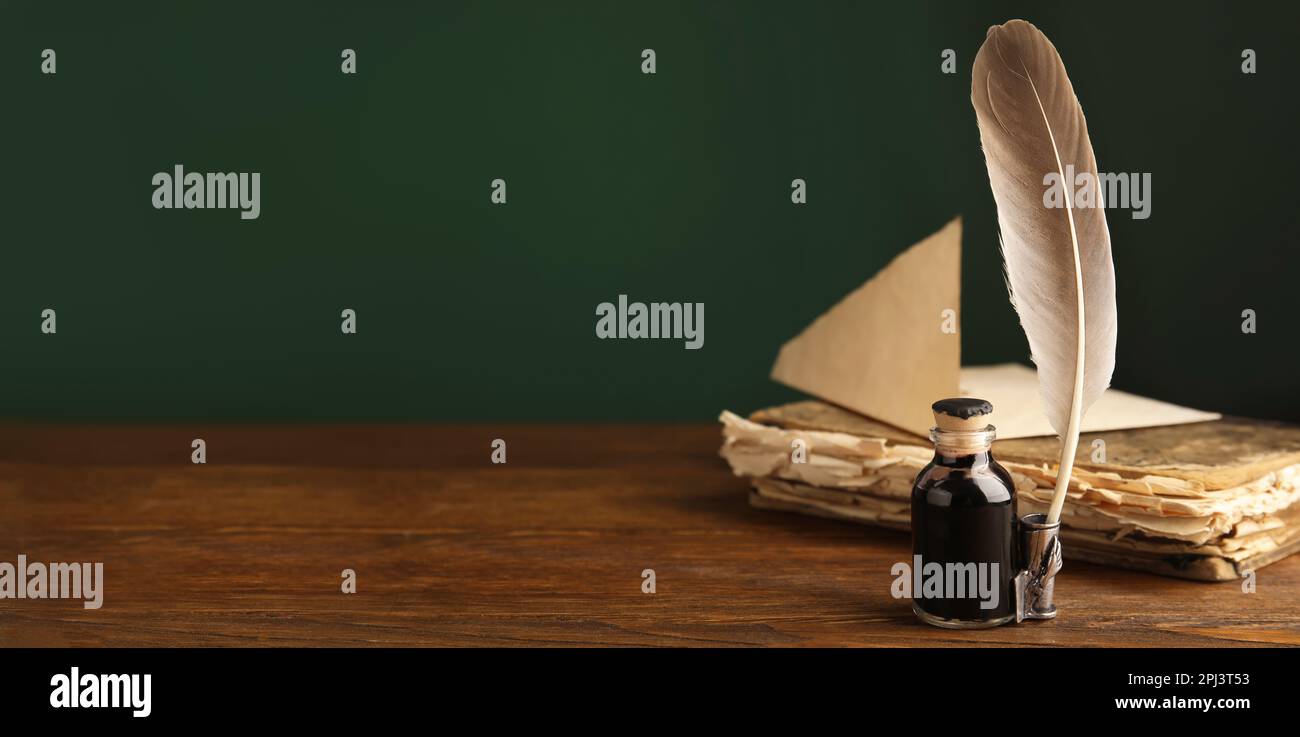 Quill, bottle of ink and old book on wooden table, space for text ...