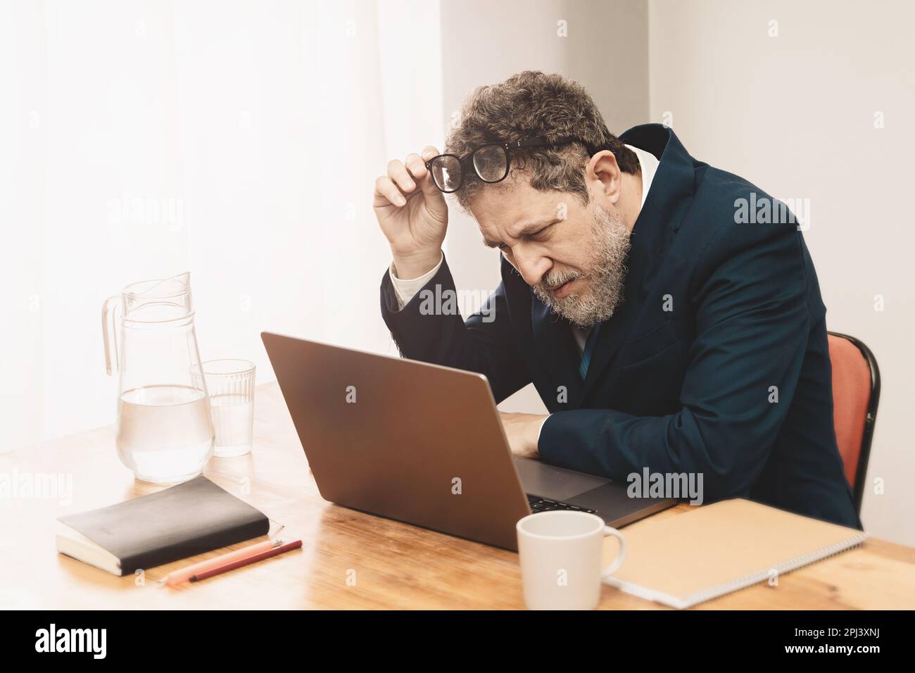 A 50-year-old man in suit and tie sits at a desk with his laptop ...