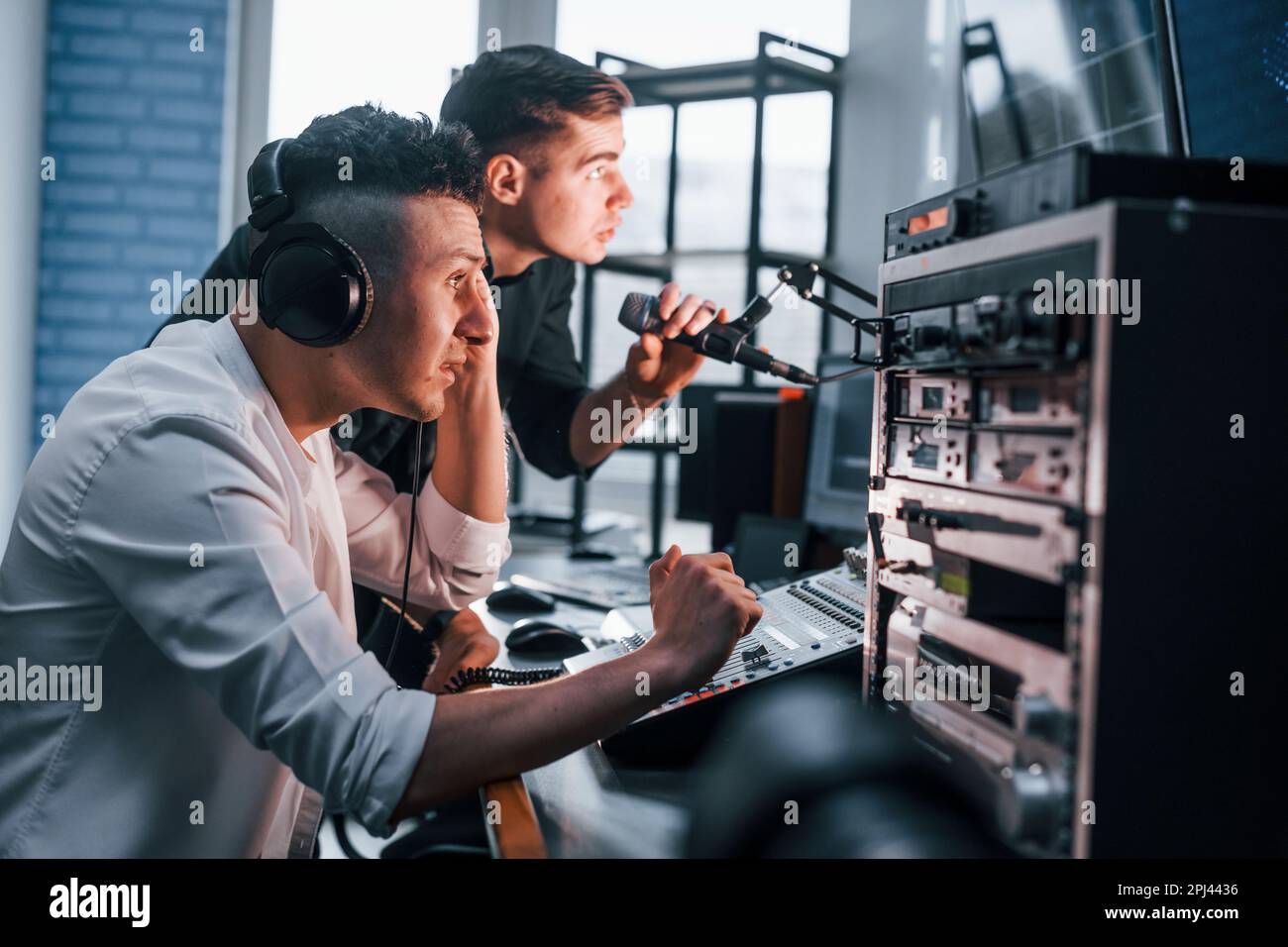 Conception of teamwork. Two guys is indoors in the radio studio is busy ...