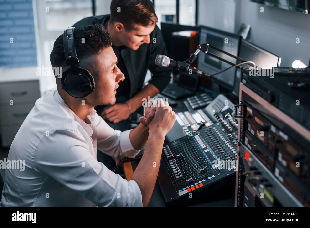 Conception of teamwork. Two guys is indoors in the radio studio is busy ...