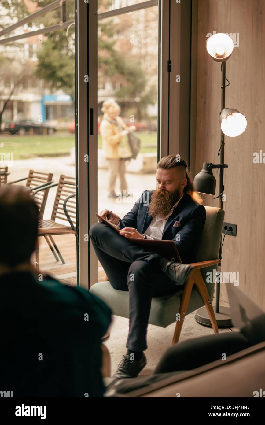 Handsome bearded man writing something on his notepad with his legs ...