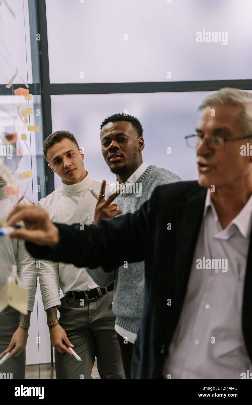 A 70s male person explaining something on the glass wall. His male ...