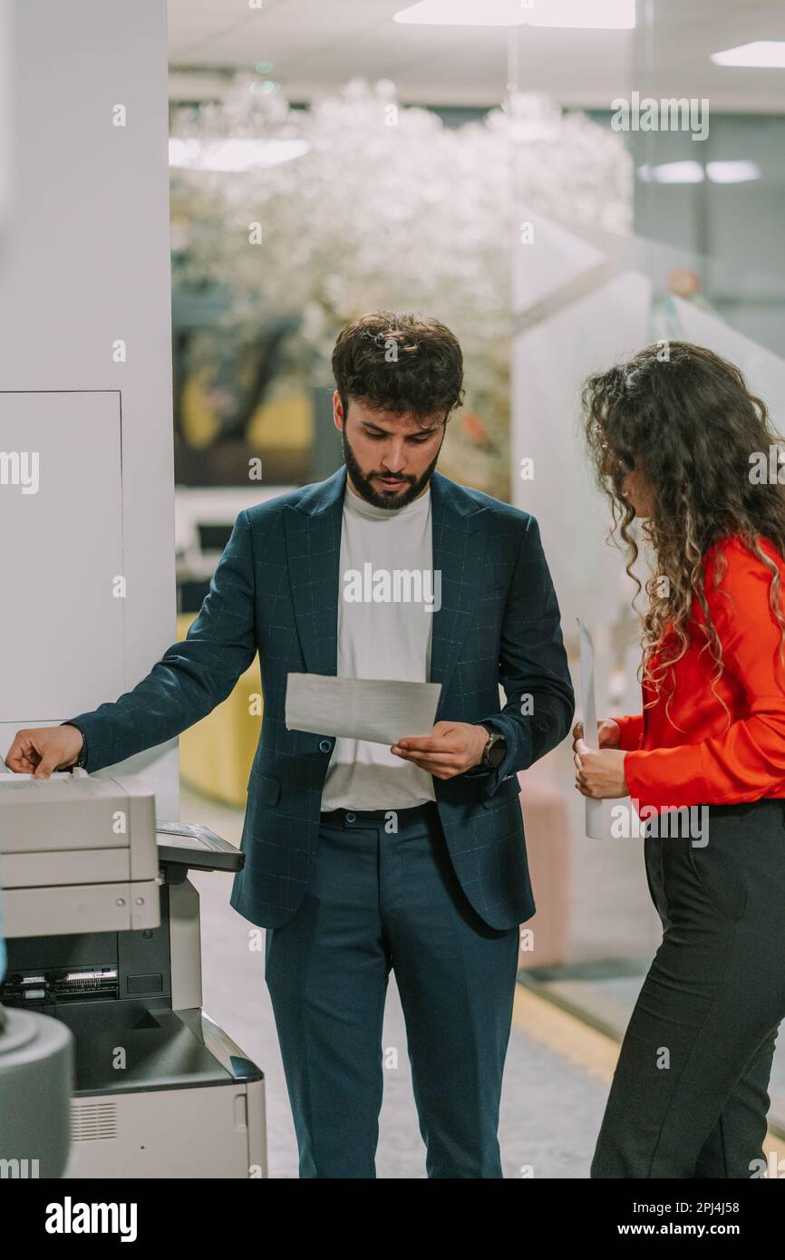 A handsome male person printing documents at the office. He is reading ...