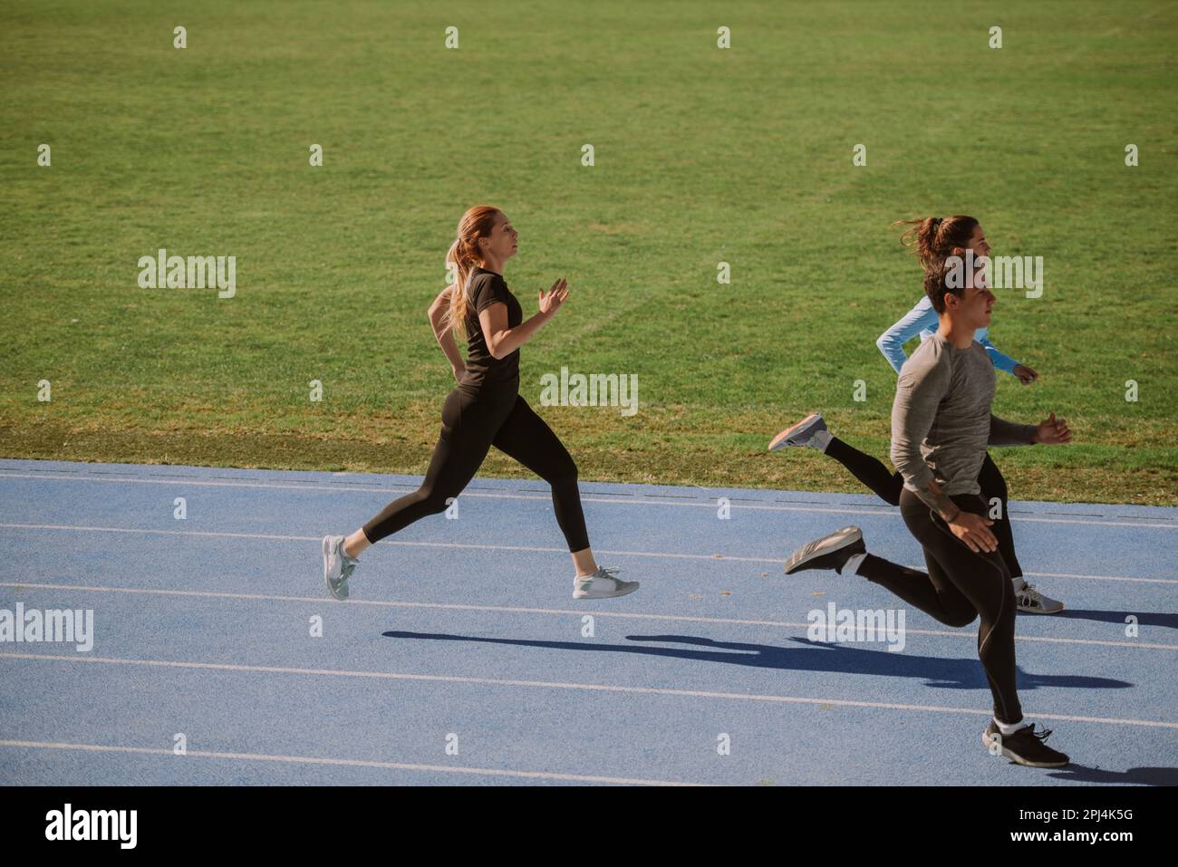 Three friends running on a blue sports track Stock Photo - Alamy