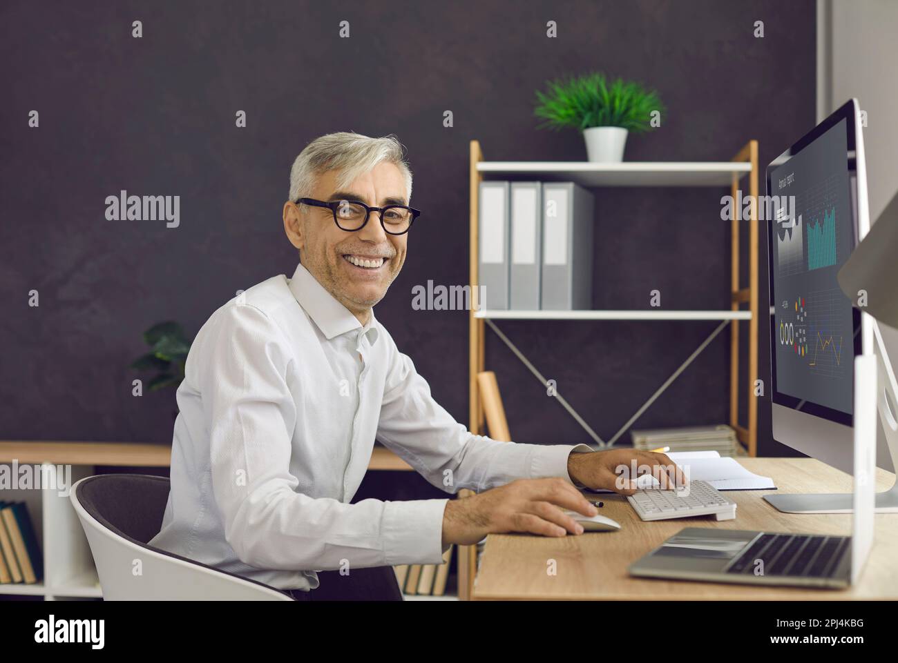 Professional male smiling in the office, analyzing graphs on the monitor screen Stock Photo - Alamy