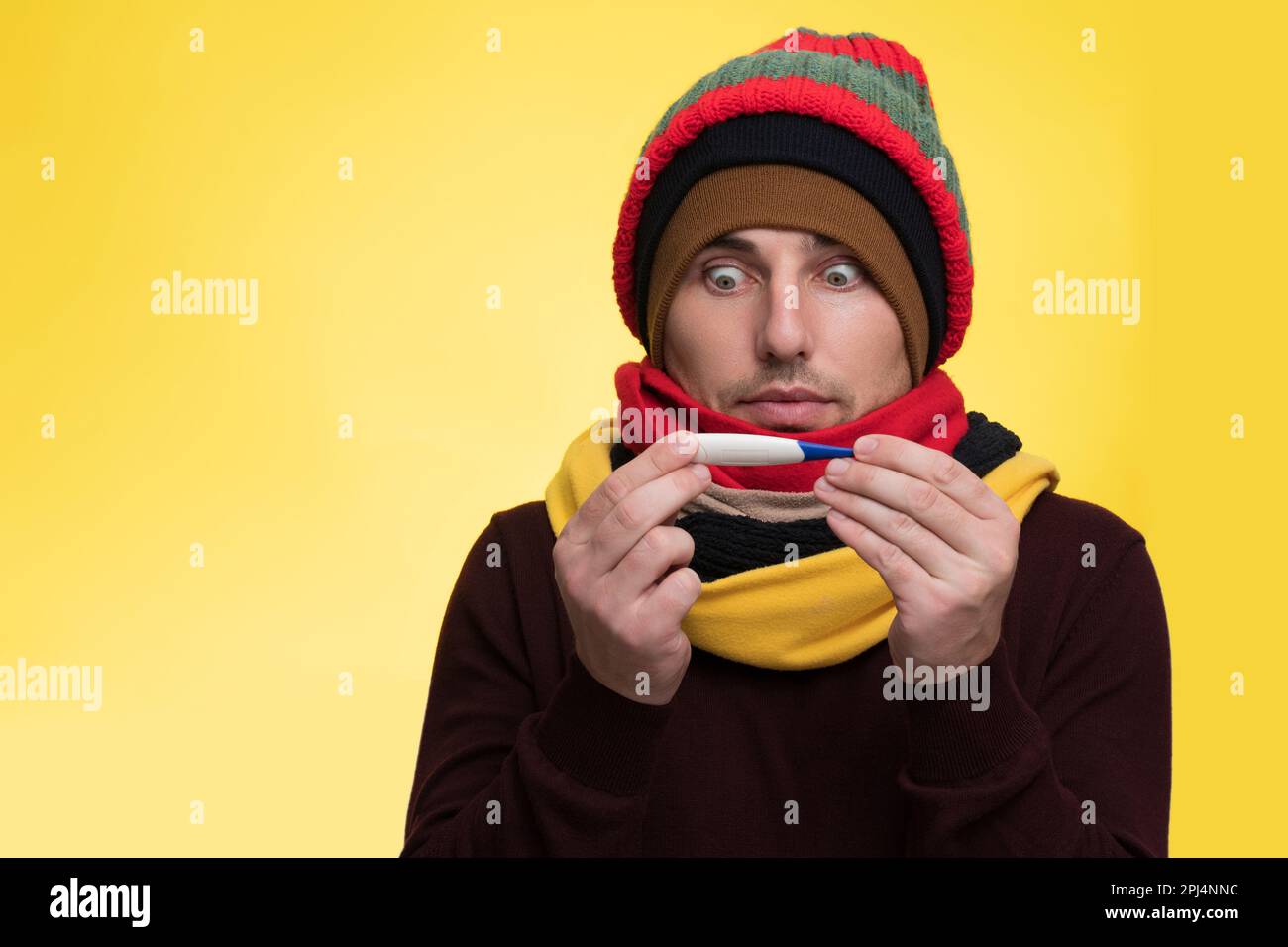 A young man in warm clothes on a yellow background holds an electronic ...