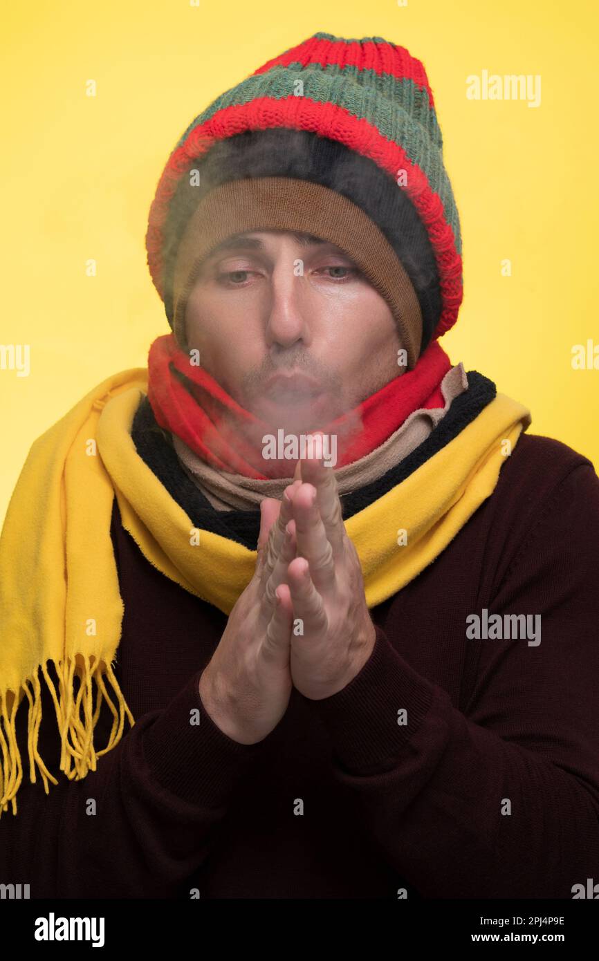 A man in warm clothes and several hats warms himself during the cold ...
