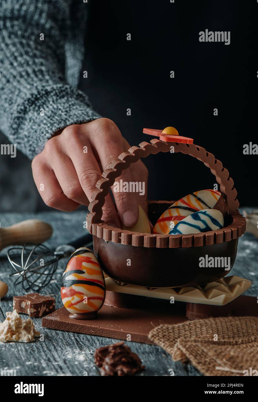 closeup of a man putting a chocolate egg into a chocolate basket, as a ...