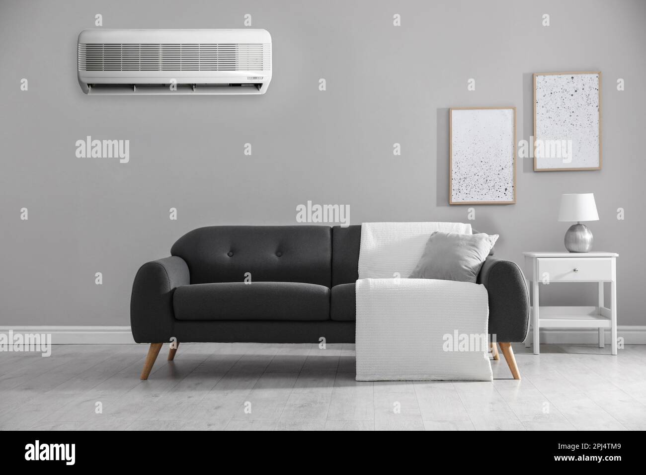 Modern air conditioner on light grey wall in room with stylish sofa ...