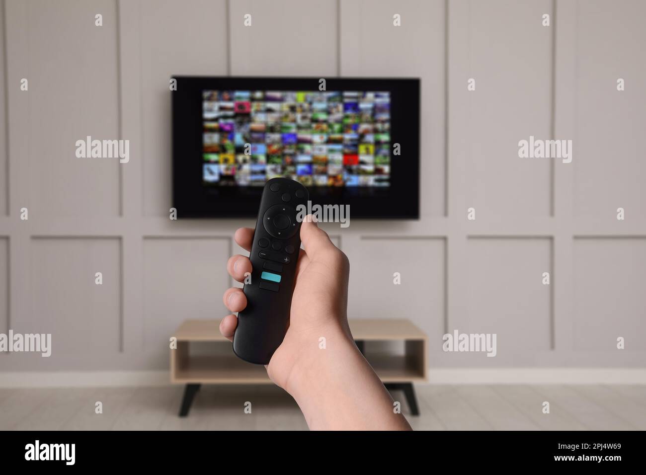 Woman with remote control changing channels while watching TV at home ...