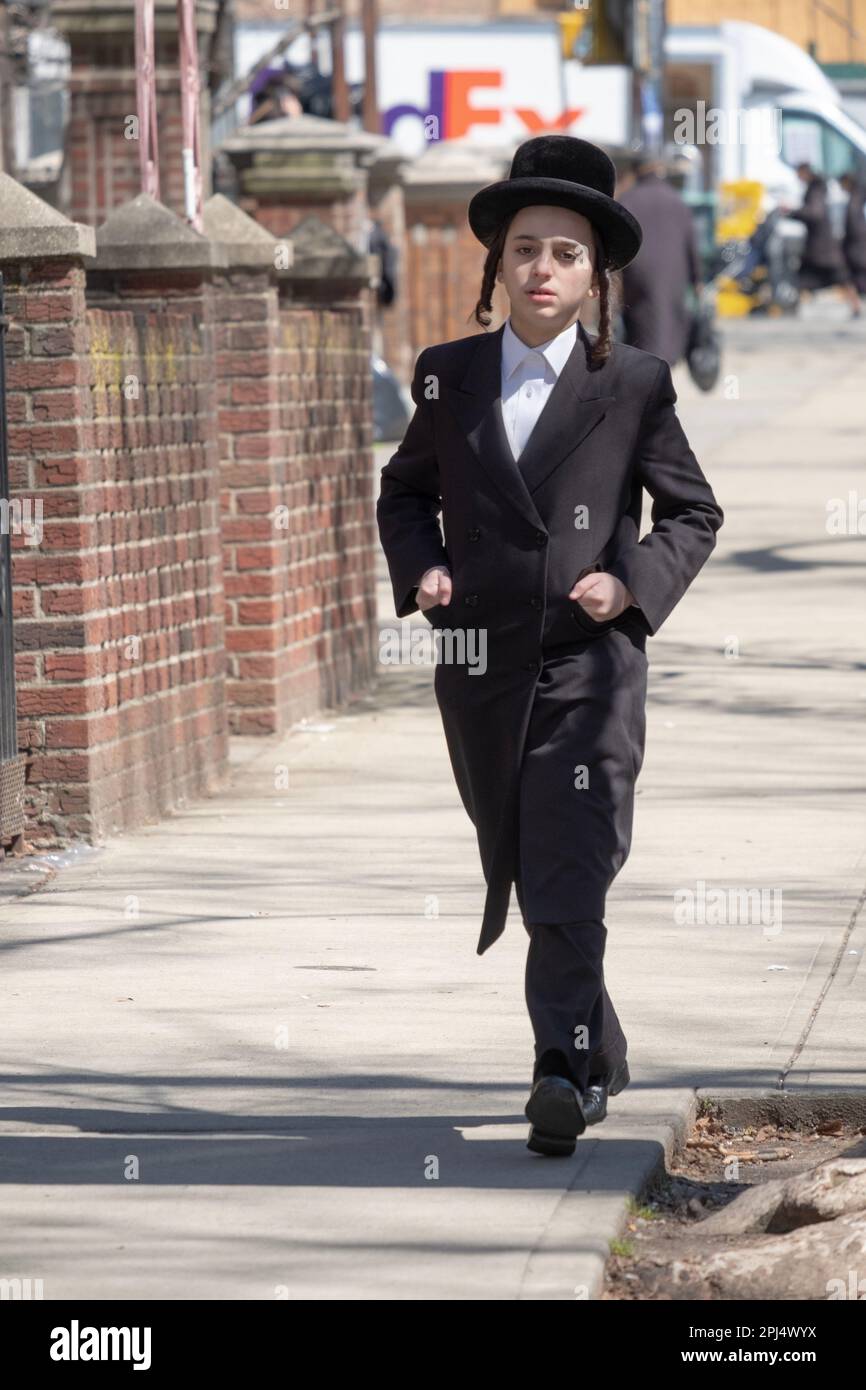 A teenage Hasidic Jewish boy walking with his hands in his pockets on a ...