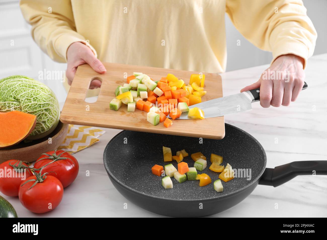 Woman pouring mix of cut vegetables into frying pan at table in kitchen ...