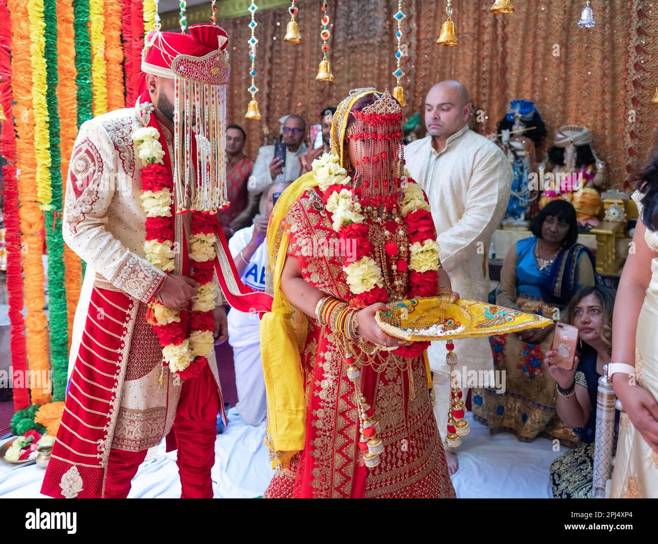 At a Hindu wedding a bride & groom connected by a red scarf march ...