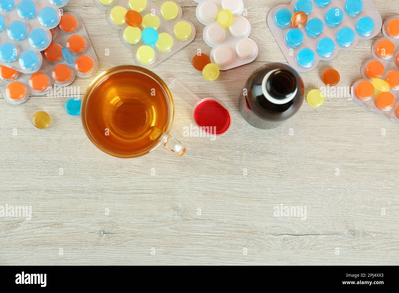 Flat lay composition with cough syrup, lozenges and cup of tea on white ...