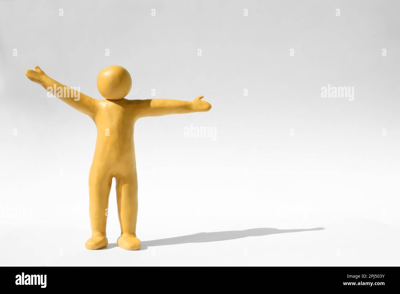 Human figure with arms wide open made of yellow plasticine on white ...