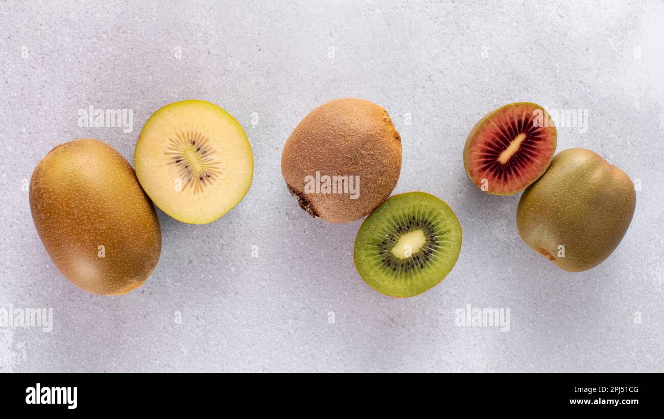 Different varieties of kiwi lie in a pile on the table. Halves of red ...