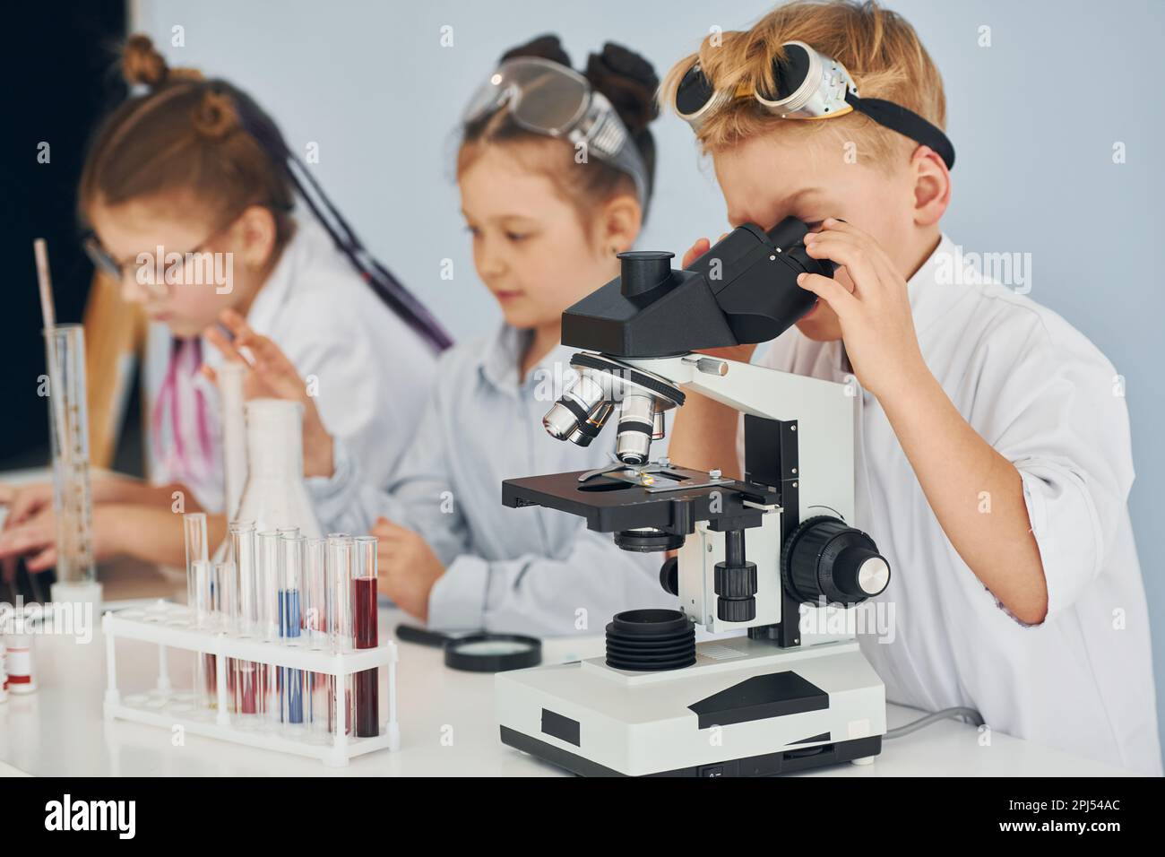 Using microscope. Children in white coats plays a scientists in lab by ...