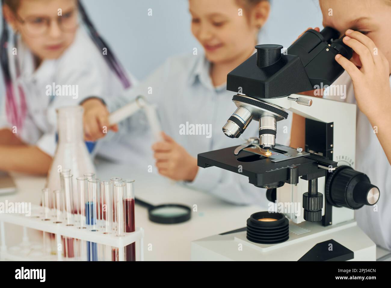 Using microscope. Children in white coats plays a scientists in lab by ...