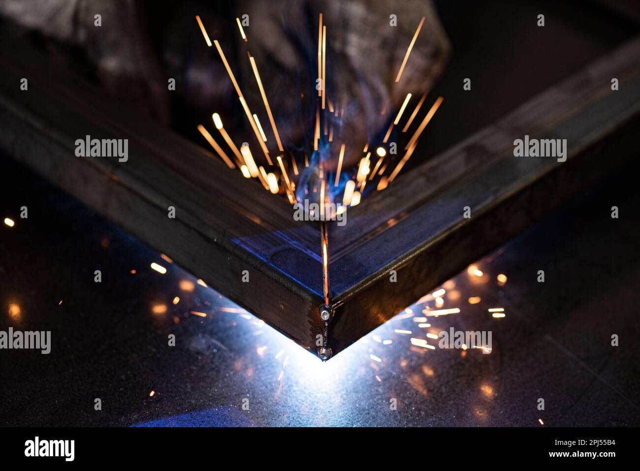 Closeup photo of metalworking in dark workshop. Welding and grinding ...