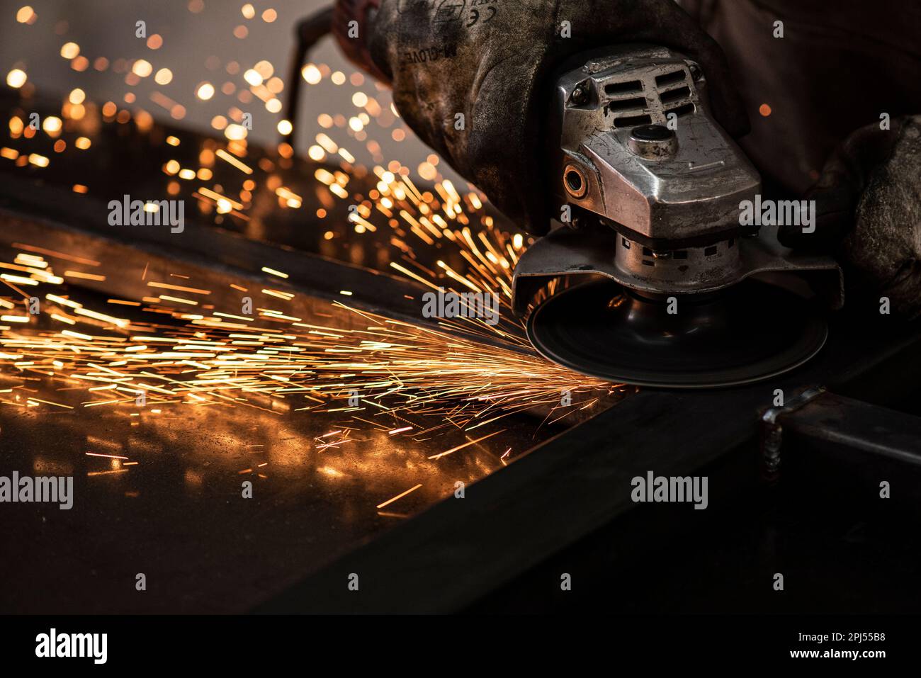 Closeup photo of metalworking in dark workshop. Welding and grinding ...