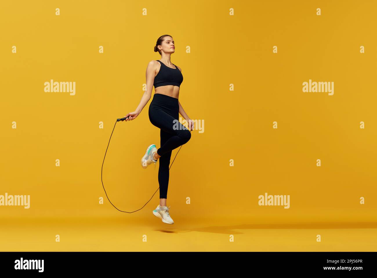 Sportive young girl with fit body training, jumping over jumping rope ...