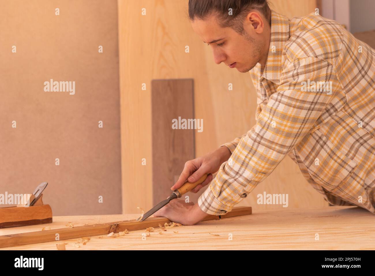 Side view of attentive male woodworker carving wood with rasp near jack ...