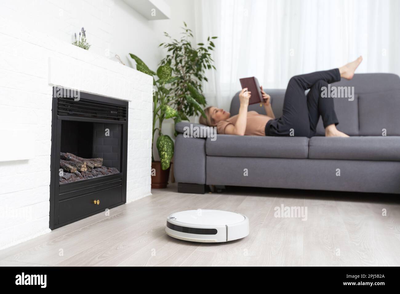 Robotic vacuum cleaner cleaning the room while woman resting on sofa ...