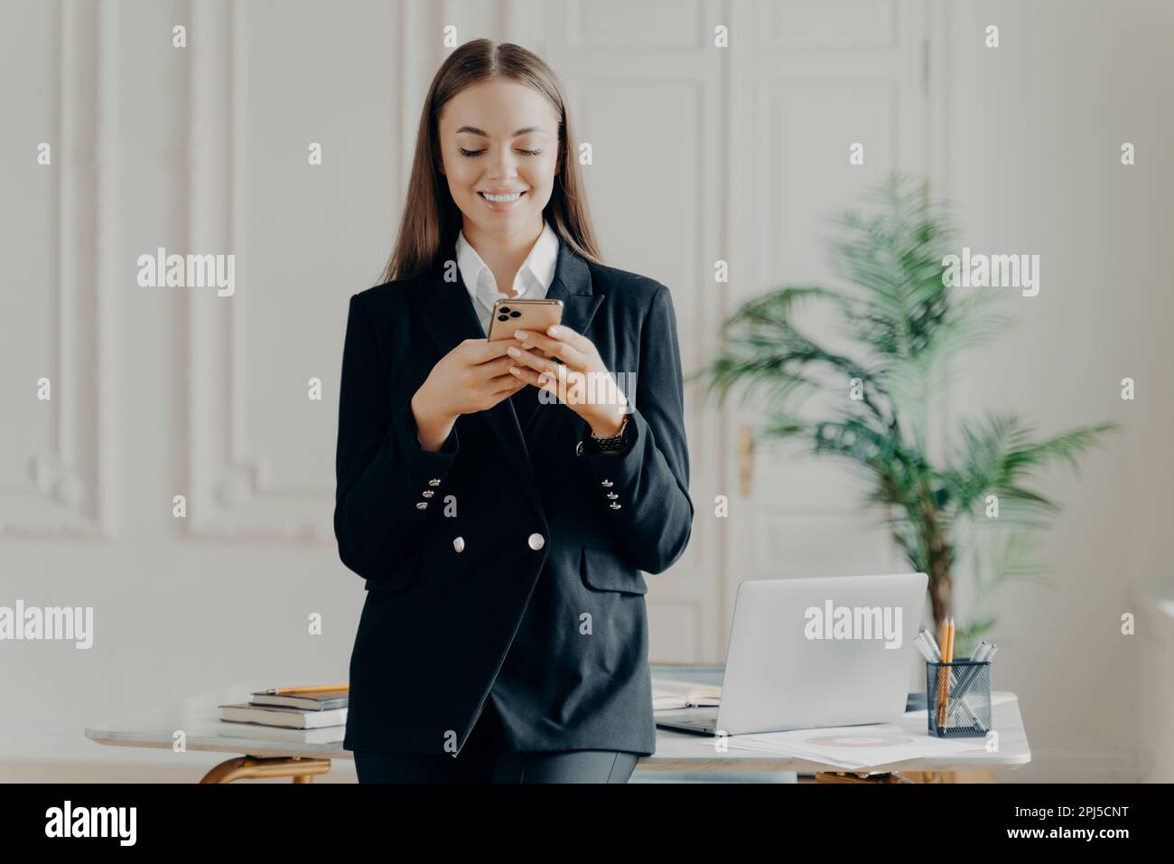 Happy professional female entrepreneur in formal suit holding phone and ...