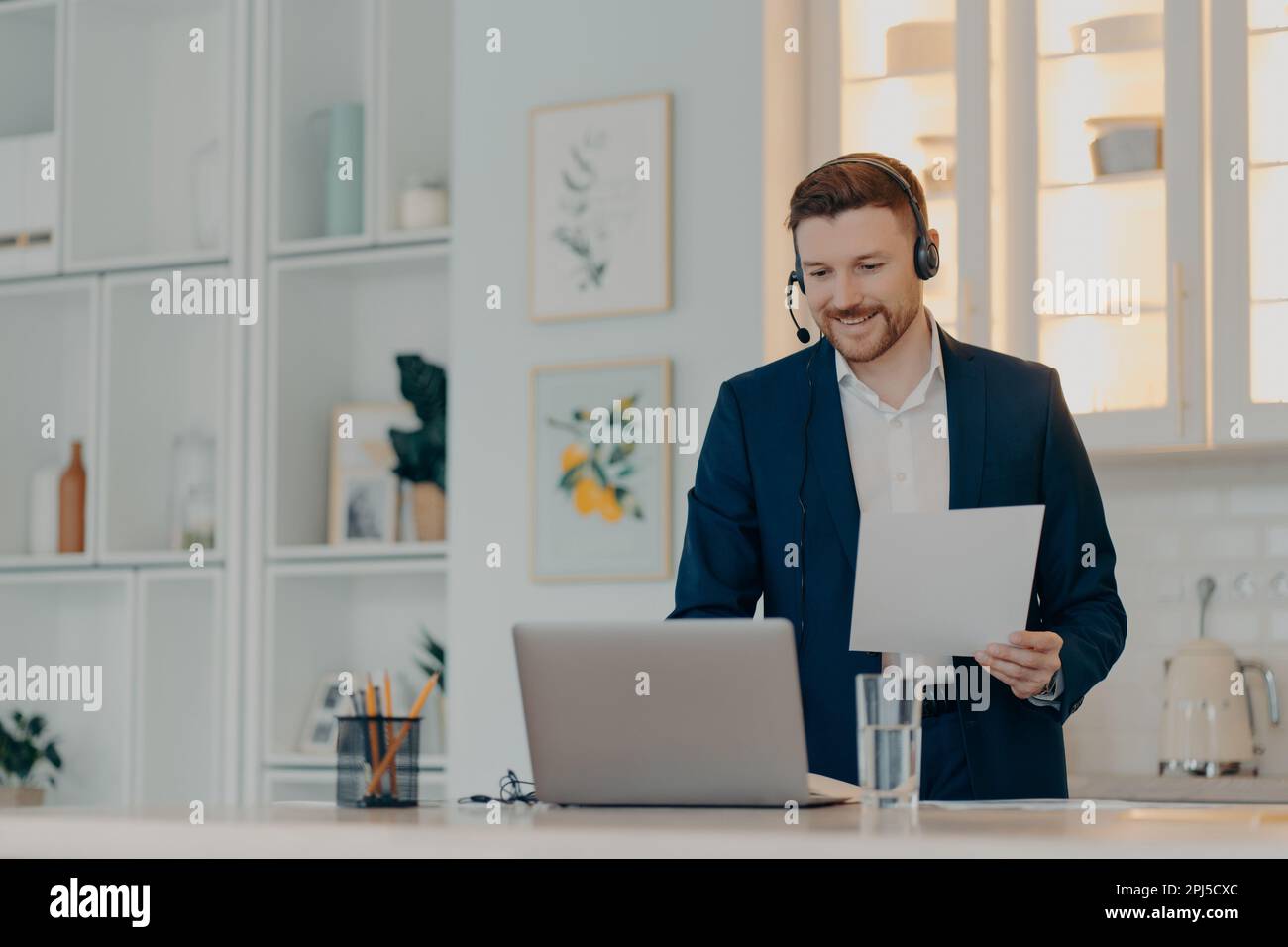 Happy young businessman wearing suit and headset working remotely from ...
