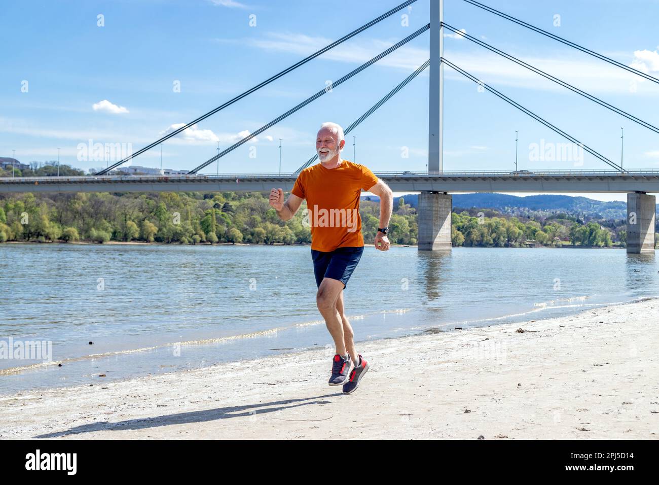 Happy energetic senior man jogging on the sand beach. Speeding by the ...