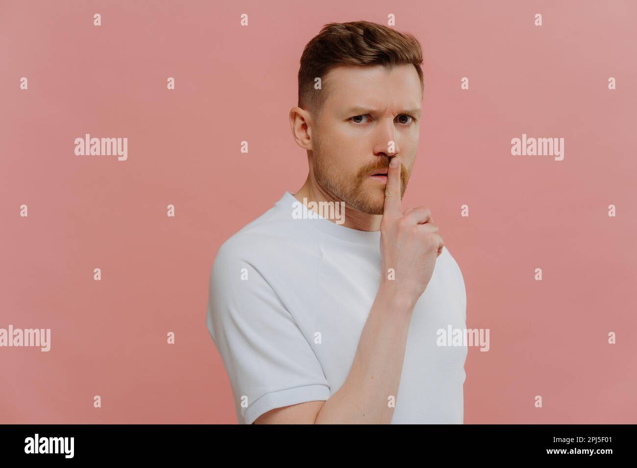 Keep it in secret. Young unshaven man in white tshirt showing silence ...