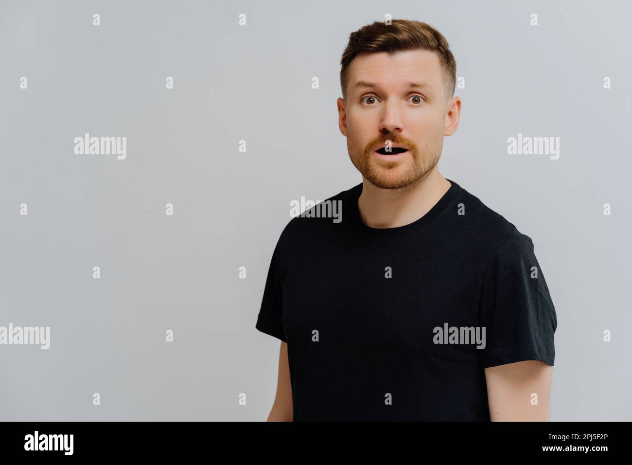 Studio shot of surprised intrigued handsome ginger man in black tshirt ...