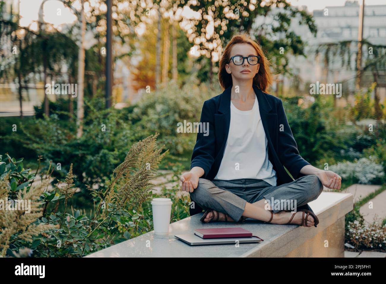 Full length shot of relaxed ginger woman meditates sits in lotus pose ...